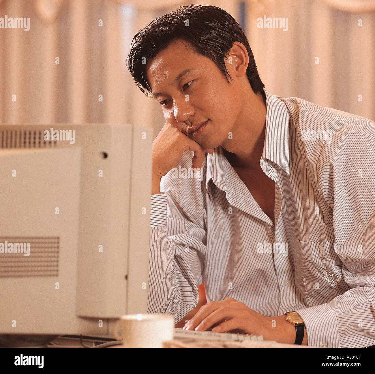 Chinese young man sitting in front of a computer thinking Stock Photo ...