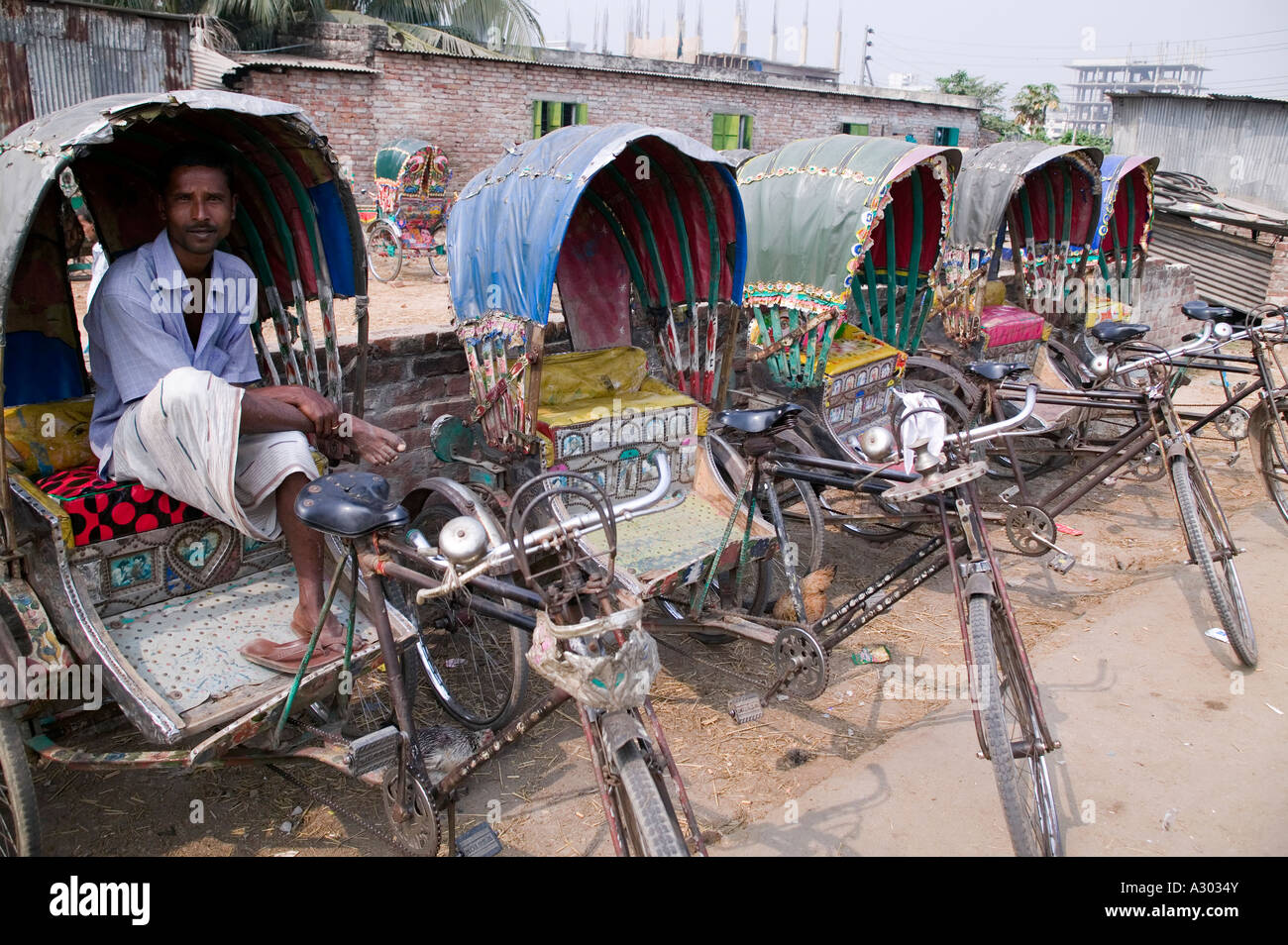 A rickshaw puller sitting on the passenger seat of a parked rickshaw in ...
