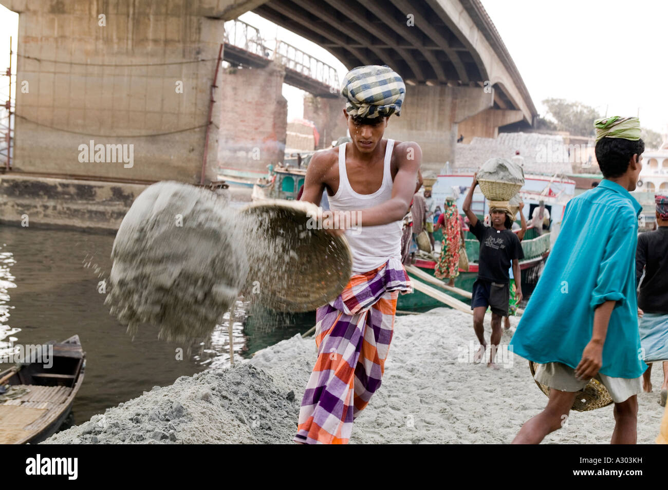 A man dumping out sand he carried from a boat to a pile on land to be ...