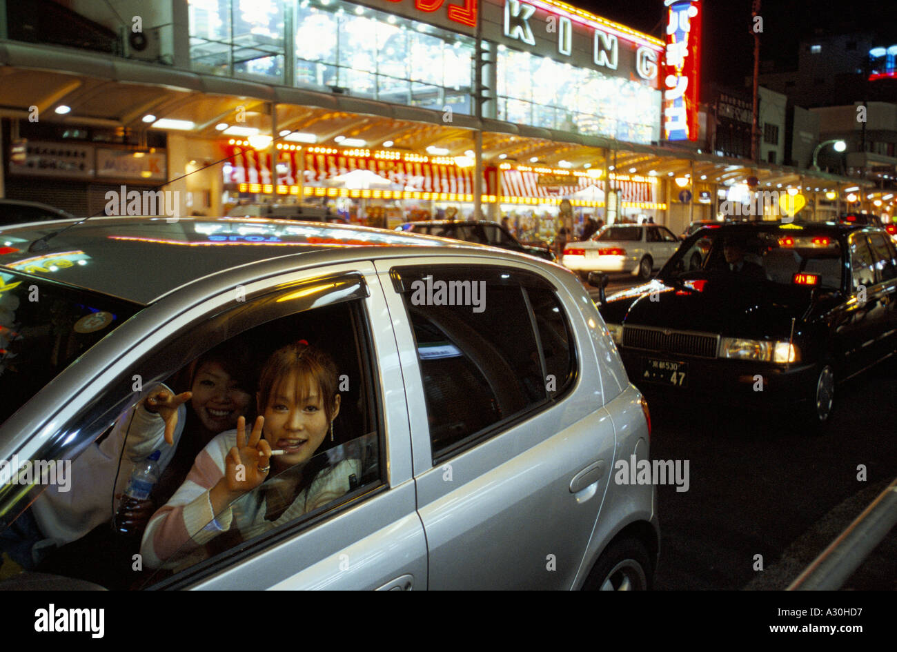 Teenage Japanese girls wave from a parked car at night in Kyoto Japan ...