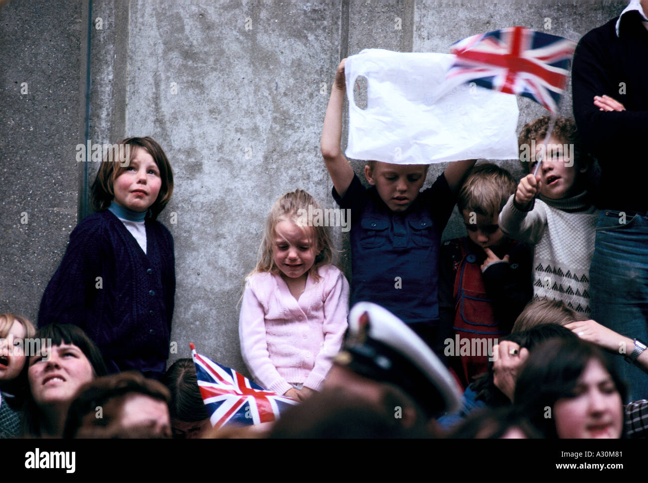 children holding aloft union jack flags and watching the QE2 sail for ...