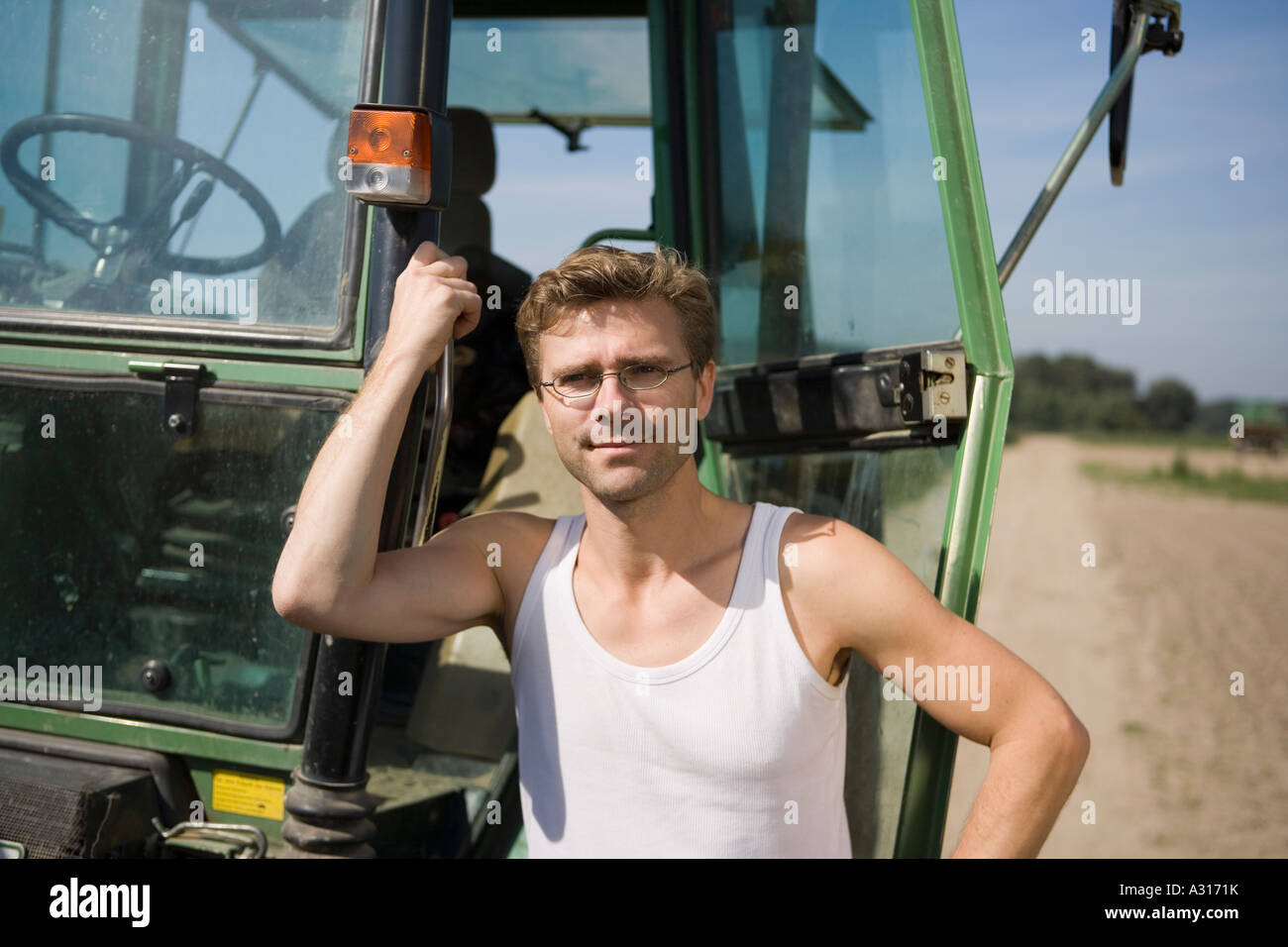Farm worker standing next to tractor in field Stock Photo - Alamy