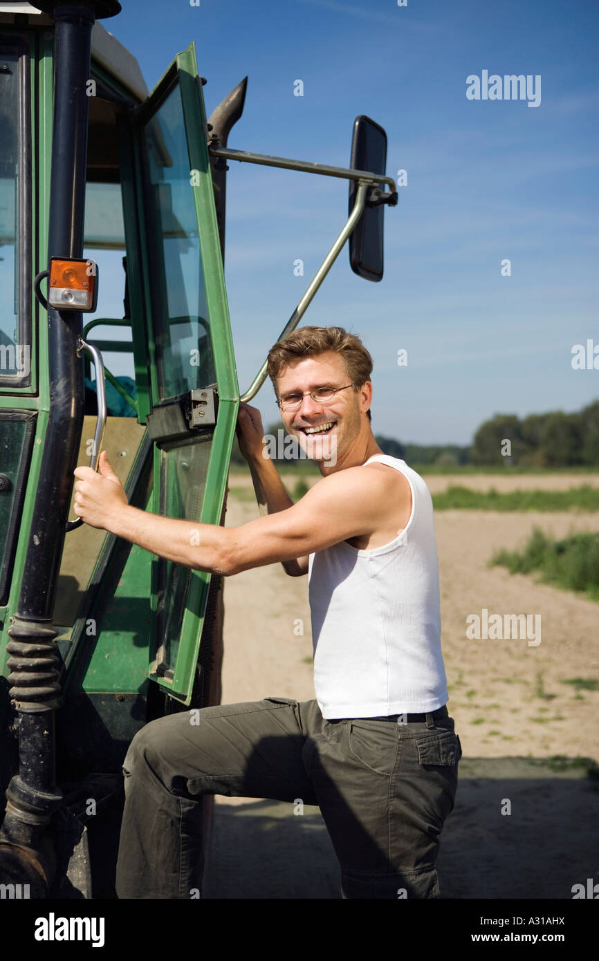 Farm worker climbing into tractor and smiling Stock Photo - Alamy