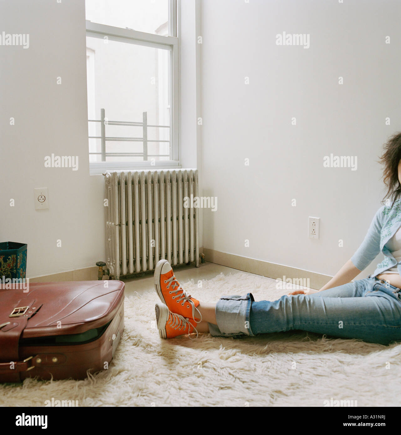 Young woman sitting on a rug with a suitcase at her feet Stock Photo ...
