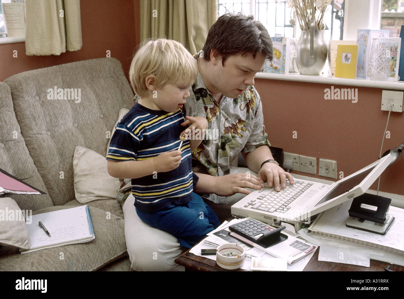 Father doing work on computer at home while tending to his child Stock ...