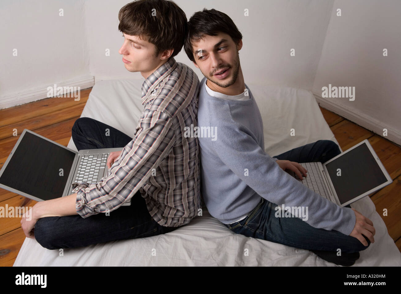 Two young men sitting back to back using laptops Stock Photo - Alamy