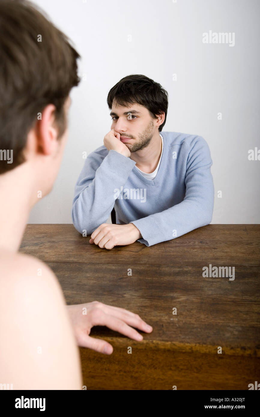 Two young men sitting opposite each other at table Stock Photo - Alamy