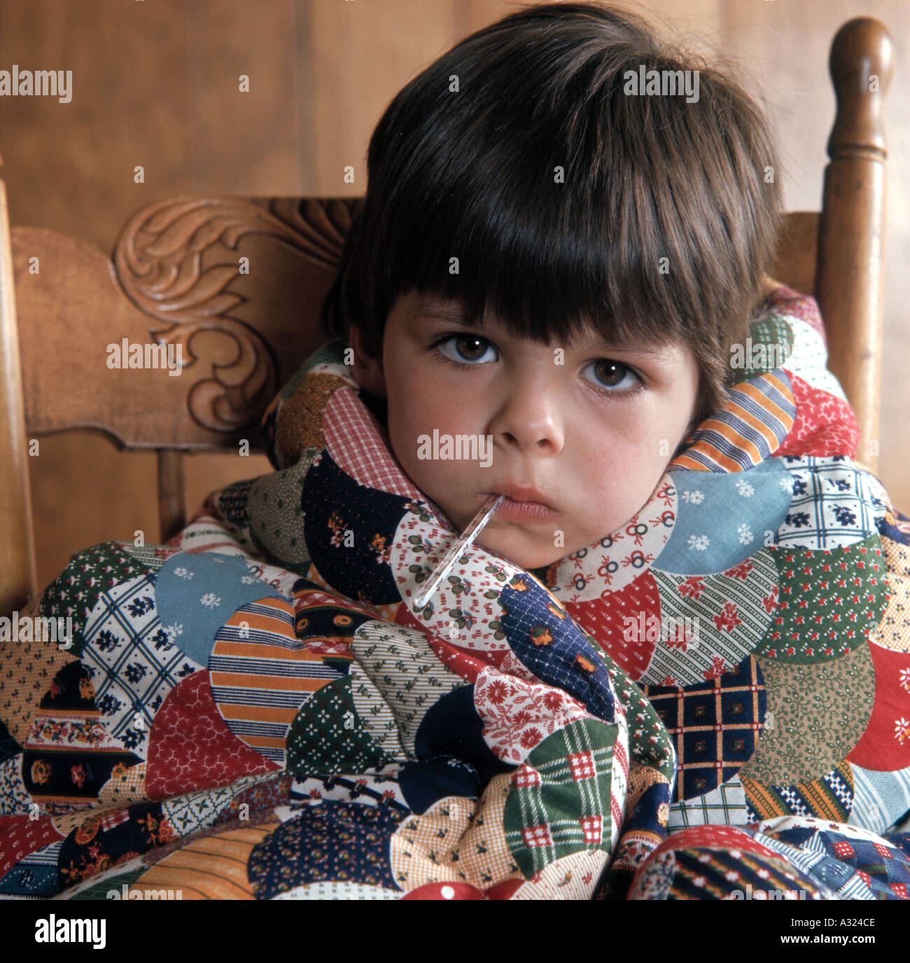Little boy sitting in a wooden rocker wrapped in a blanket with a ...