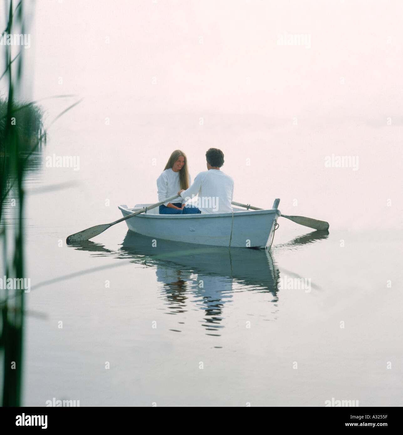 A teenage boy and girl take a romantic ride on the water in a rowboat ...