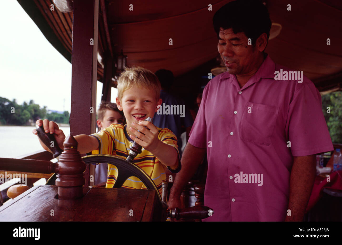Boy steers rice barge in Ayuthaya, Thailand, watched over by local Thai ...