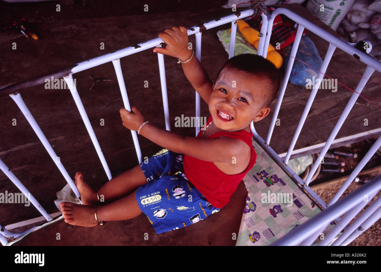 Smiling happy Thai baby suspended in hanging cot outdoors on salt farm ...