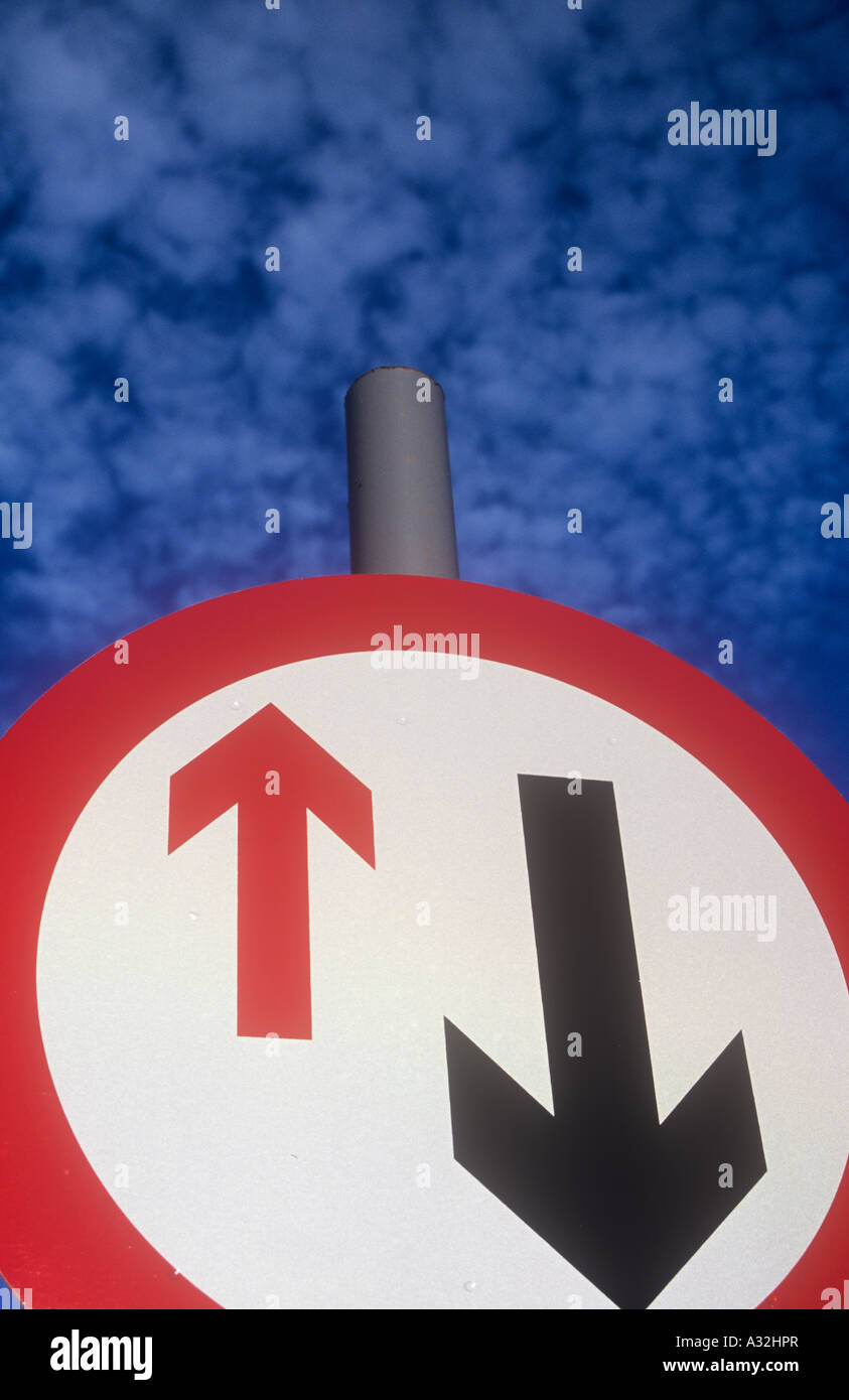 Circular red and white sign with black and red arrows against blue sky ...
