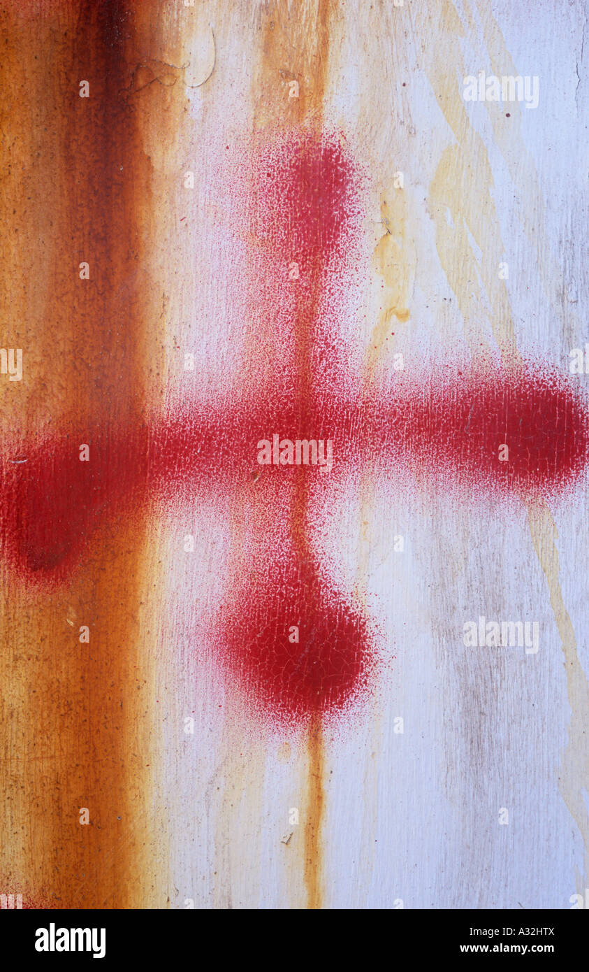 Close up of hasty spray-painted graffiti Plus sign in red on rust ...