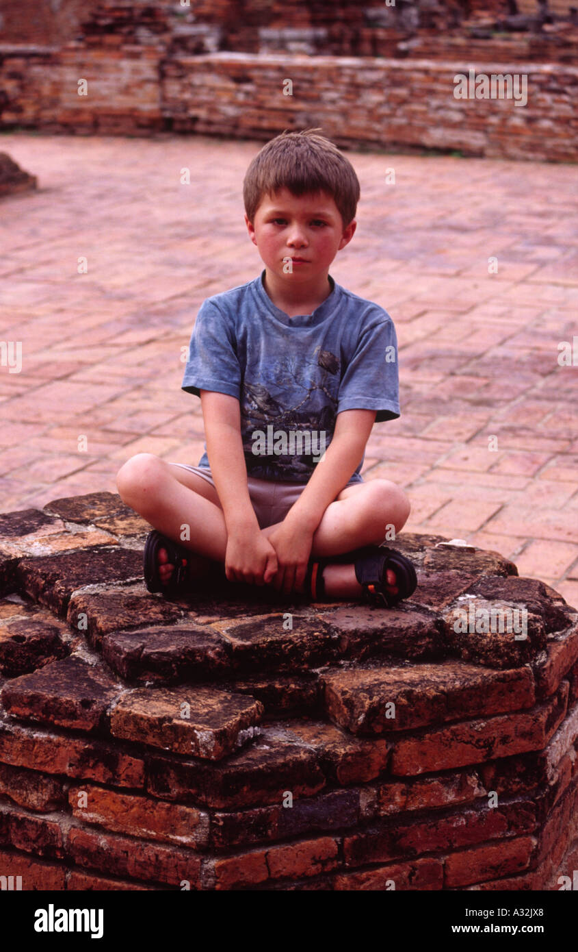 European boy pretends to be a Buddha statue, sitting on plinth in ...