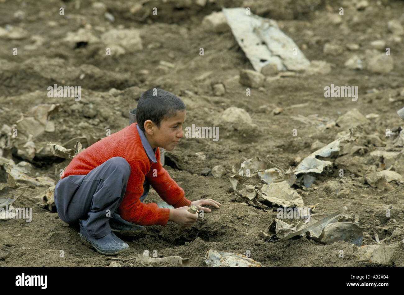 A boy digging at a bomb-site with pieces of scrap metal scattering ...