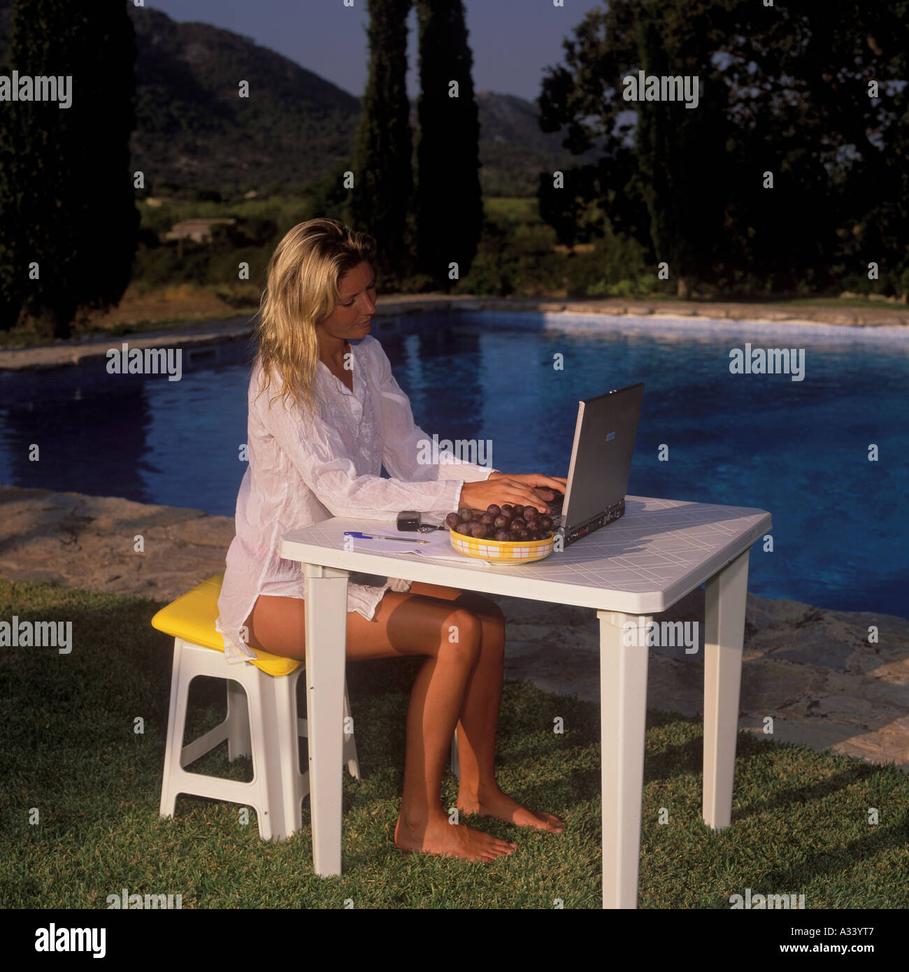 Young lady using laptop computer by the side of the swimming pool of a ...