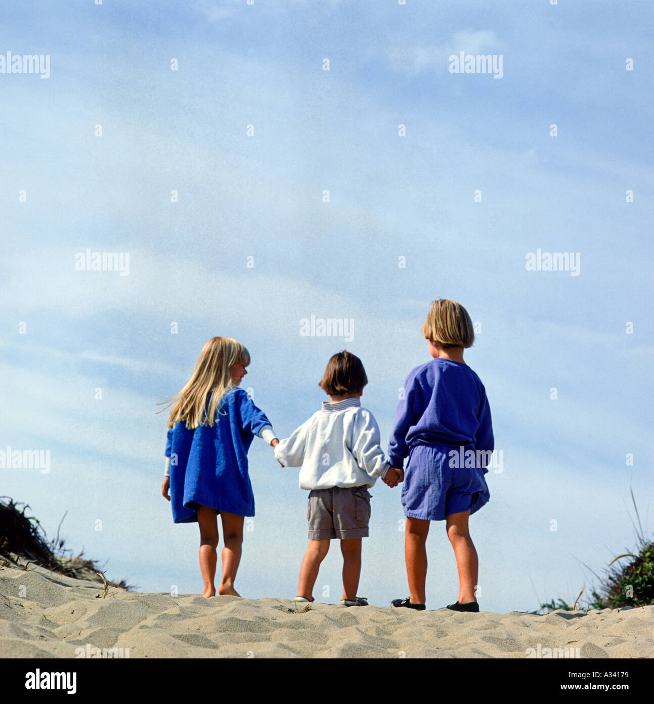 View from behind three young children one girl and two boys hold hands ...