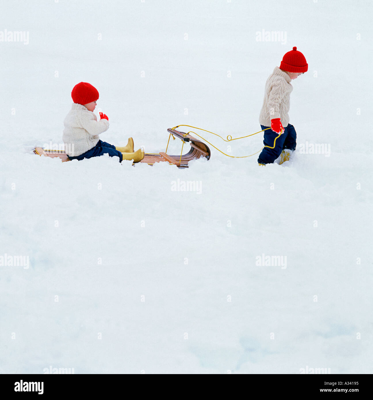 A young child pulling another child on a toboggan type sled through the ...