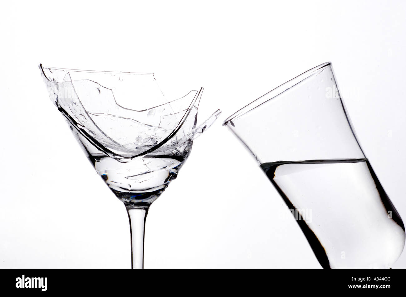 Broken Martini glass and a half full glass of water on a white ...