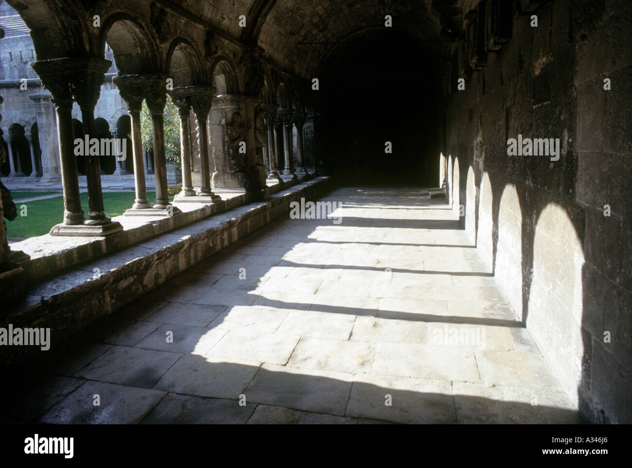A cloister in France is lit by the afternoon sun and it's arches are ...