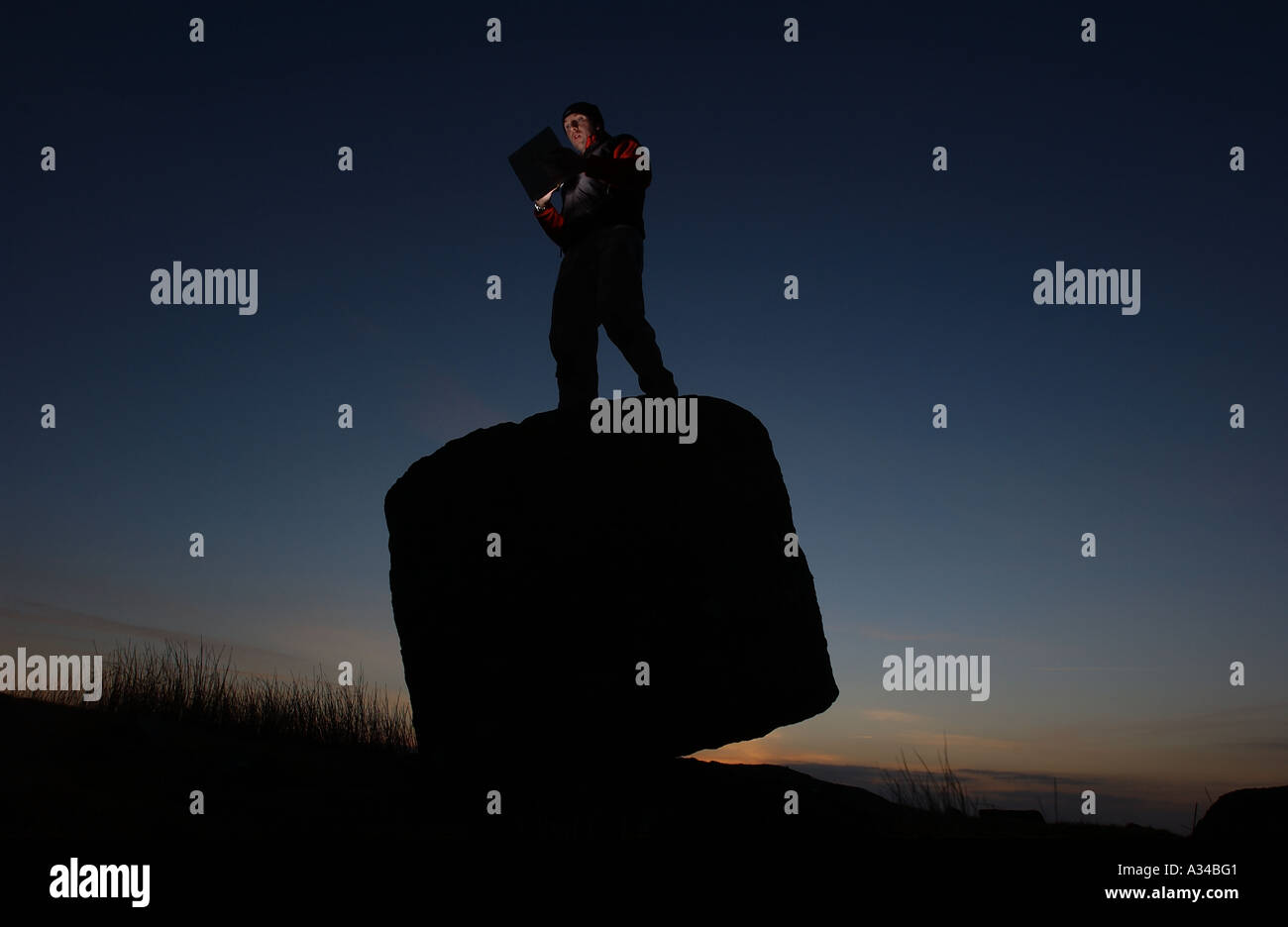 man on large boulder reading using torch headlamp at sunset on ...