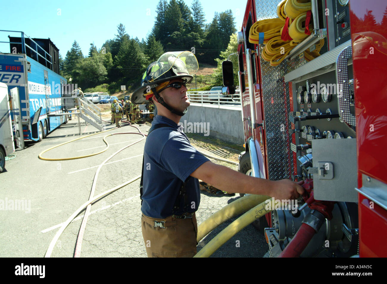 A firefighter operates the pump panel on a fire engine as other ...