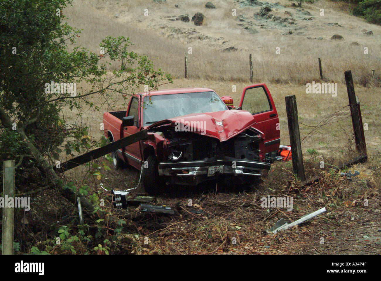 A red car rests in a field after hitting a tree flying over a barbed ...