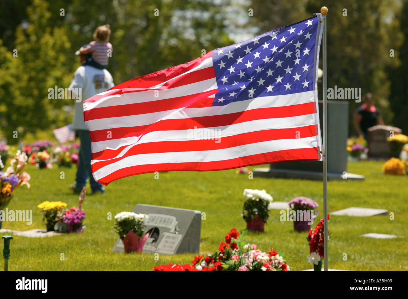 American flag at a cemetery with a father and toddler, headstones and ...