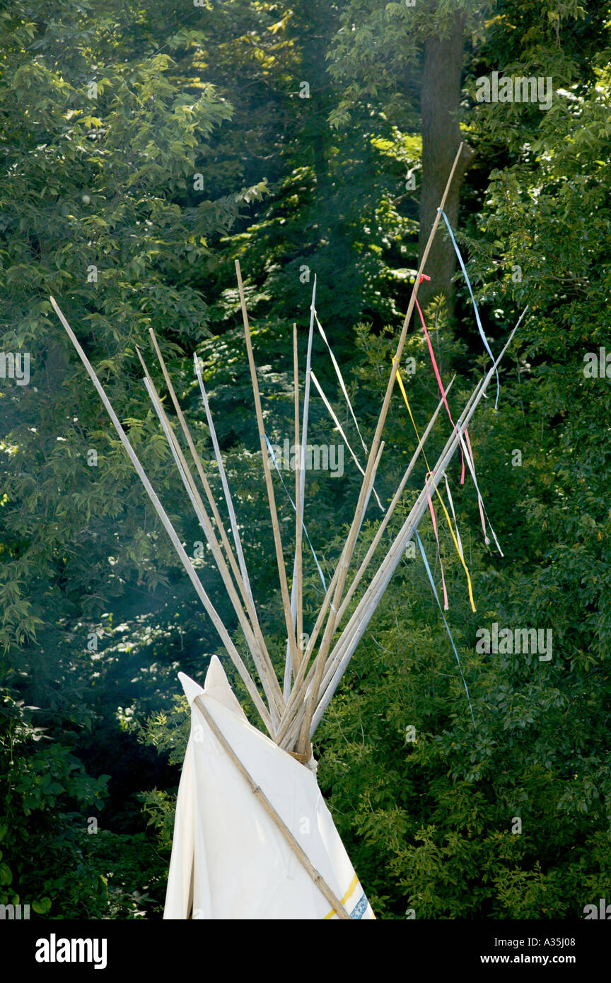 Top of a white teepee with poles and streamers with green trees in the ...