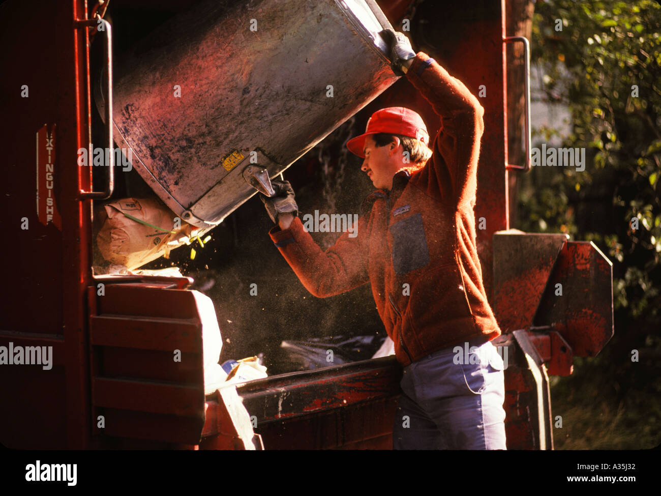 A garbage man dumps the contents of a large garbage can into the back ...