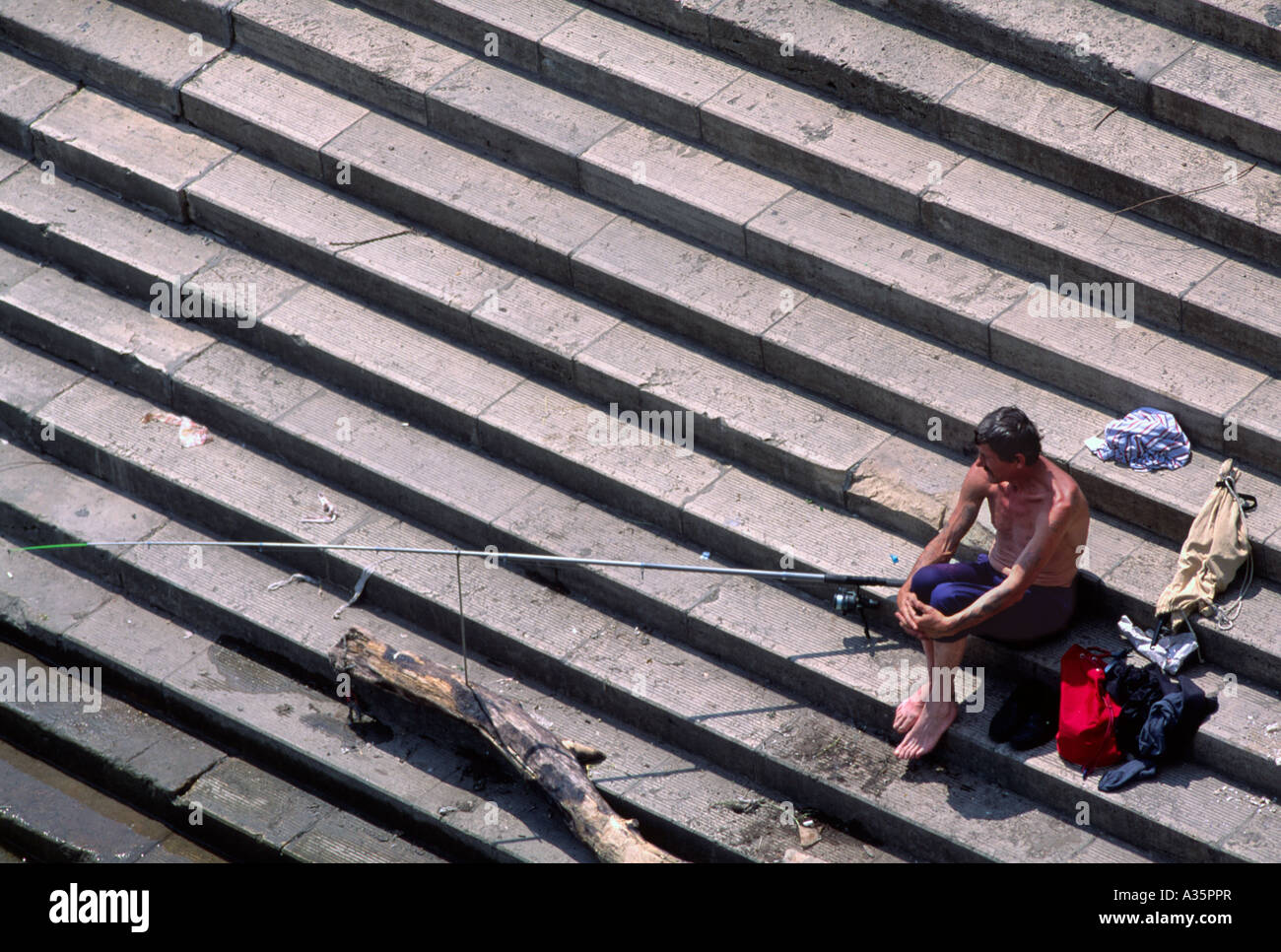 A fisherman sitting on stairs on the bank of the river Danube in ...