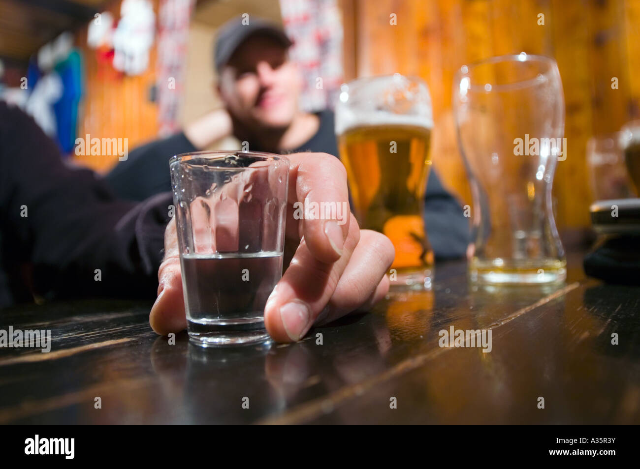 a hand holding a glass of vodka next to a large glass of beer with a ...