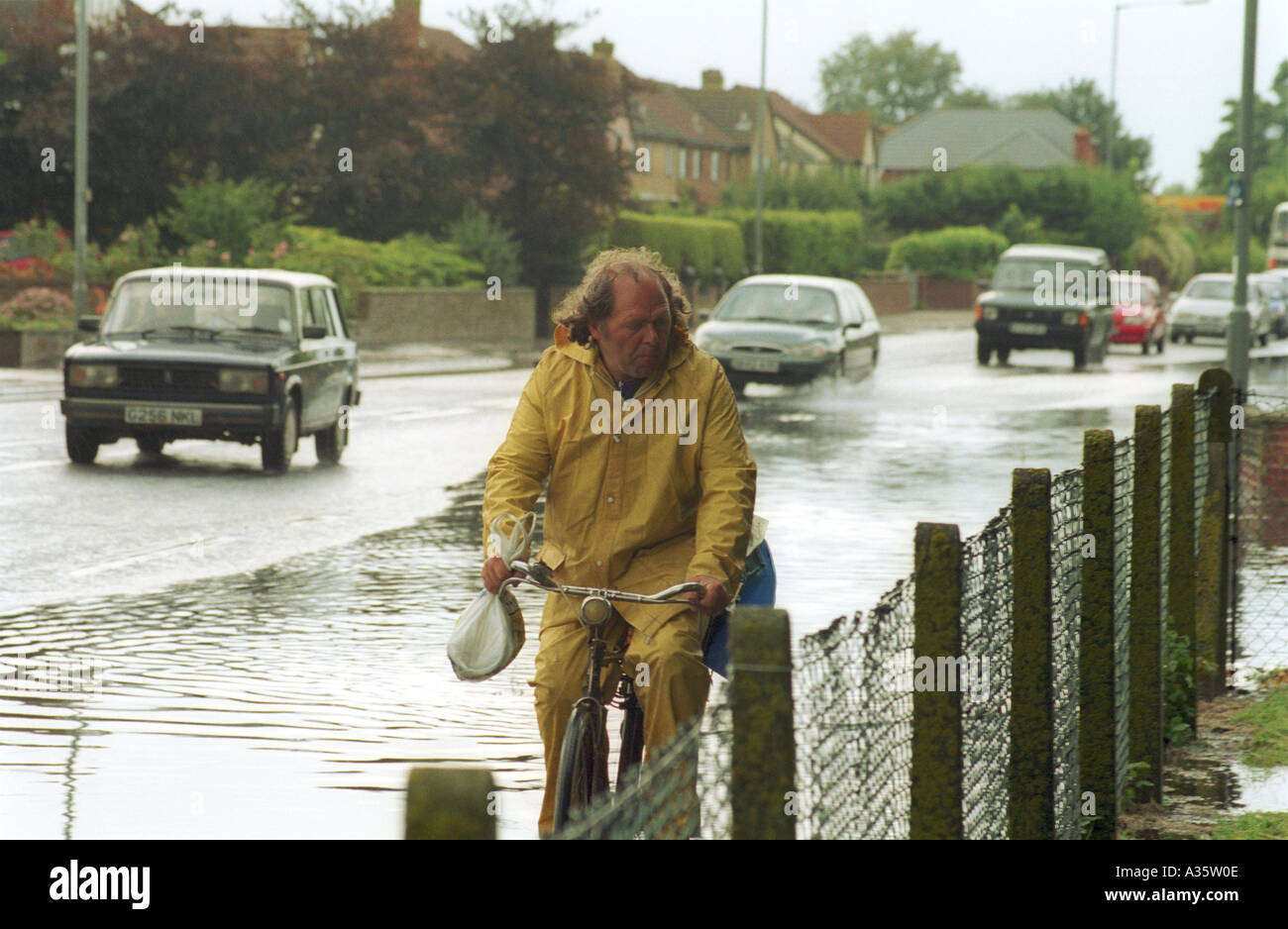 Man in yellow raincoat cycles along flooded Caister Road at Great ...