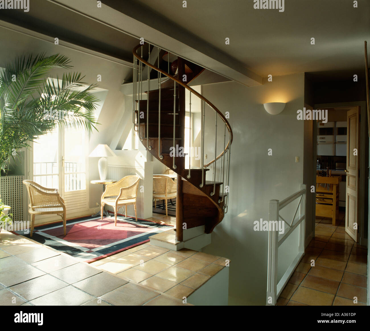 Spiral staircase onto landing with chairs and pink rug on tiled floor ...