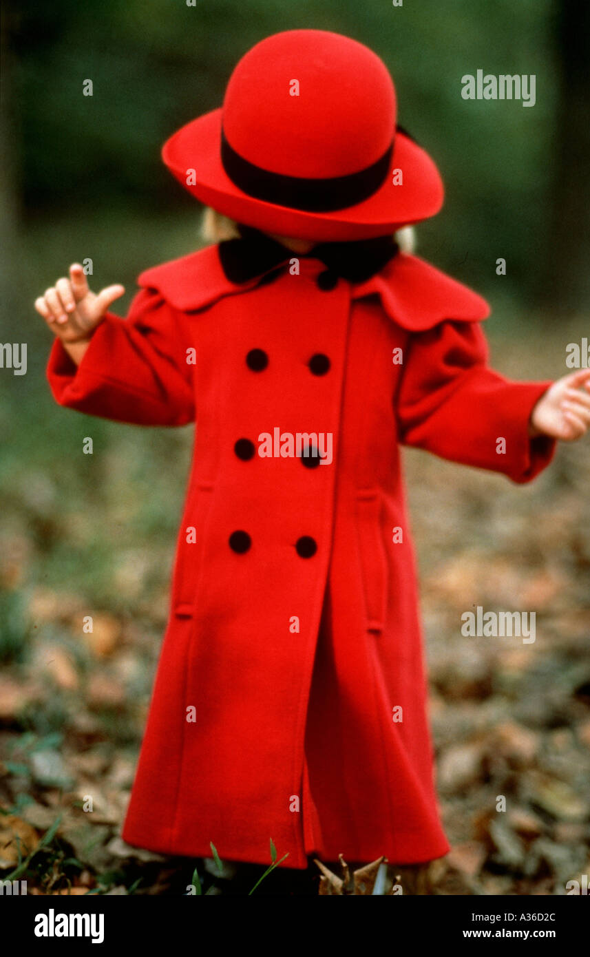 A young girl wearing a bright red winter coat and hat looks off balance ...