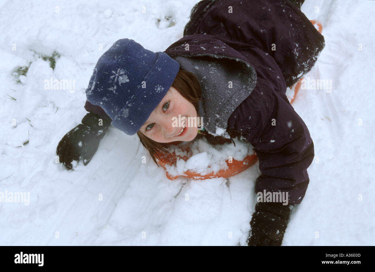 A young girl is riding a sled on her belly as she smiles up at the ...