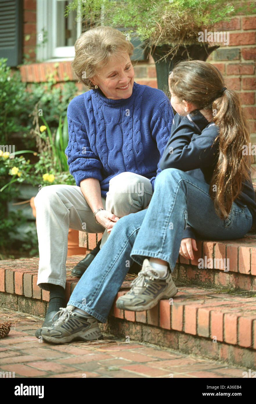 A grandmother sits on the steps of her house talking to her pre ...