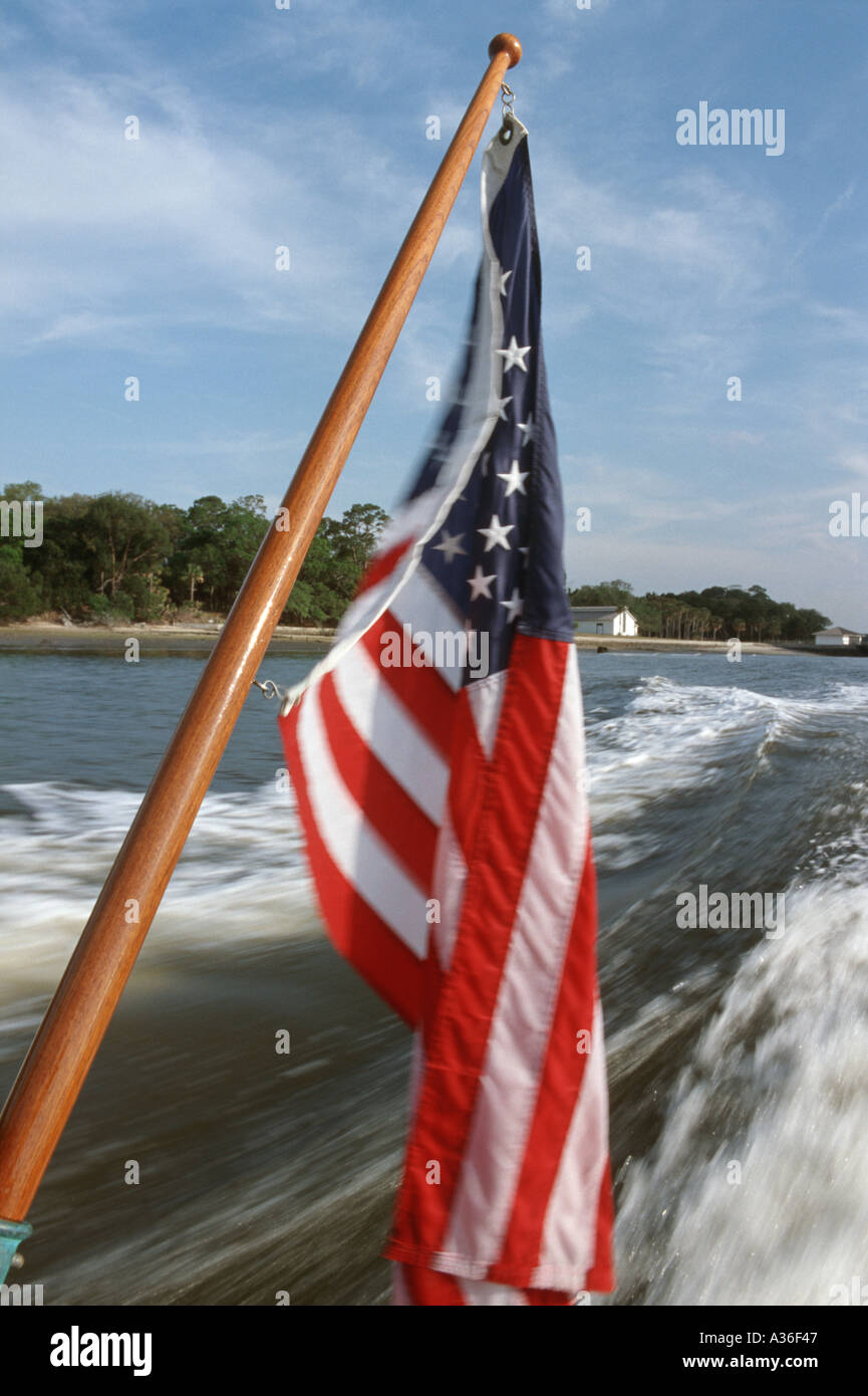 An AMerican flag is hanging off the back of a boat as it rides over the ...