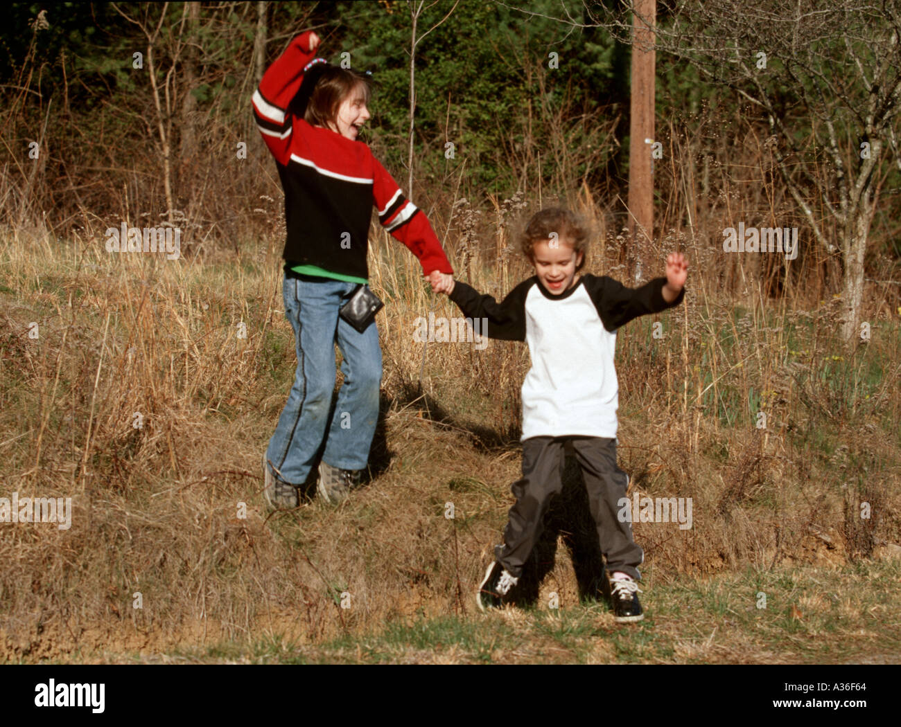 Two girls hold hands as they jump off a ledge into the tall grass in a ...