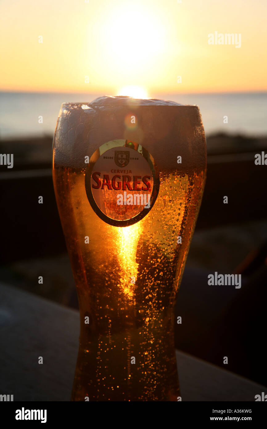the sun sets behind a full glass of beer on a beach in portugal Stock ...