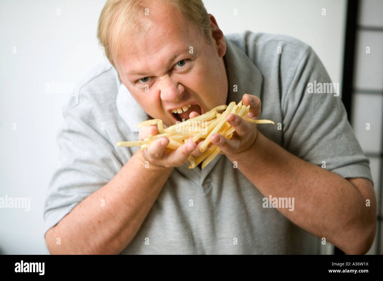 A hungry man is gorging on great handfuls of chips or French fries with ...