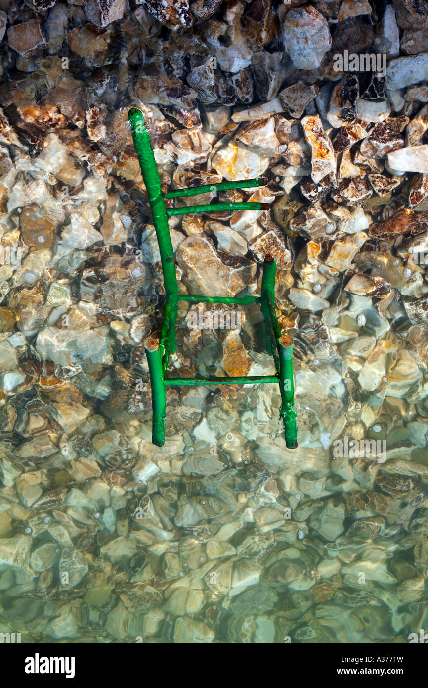 Broken green chair lying underwater on rocky beach Stock Photo - Alamy