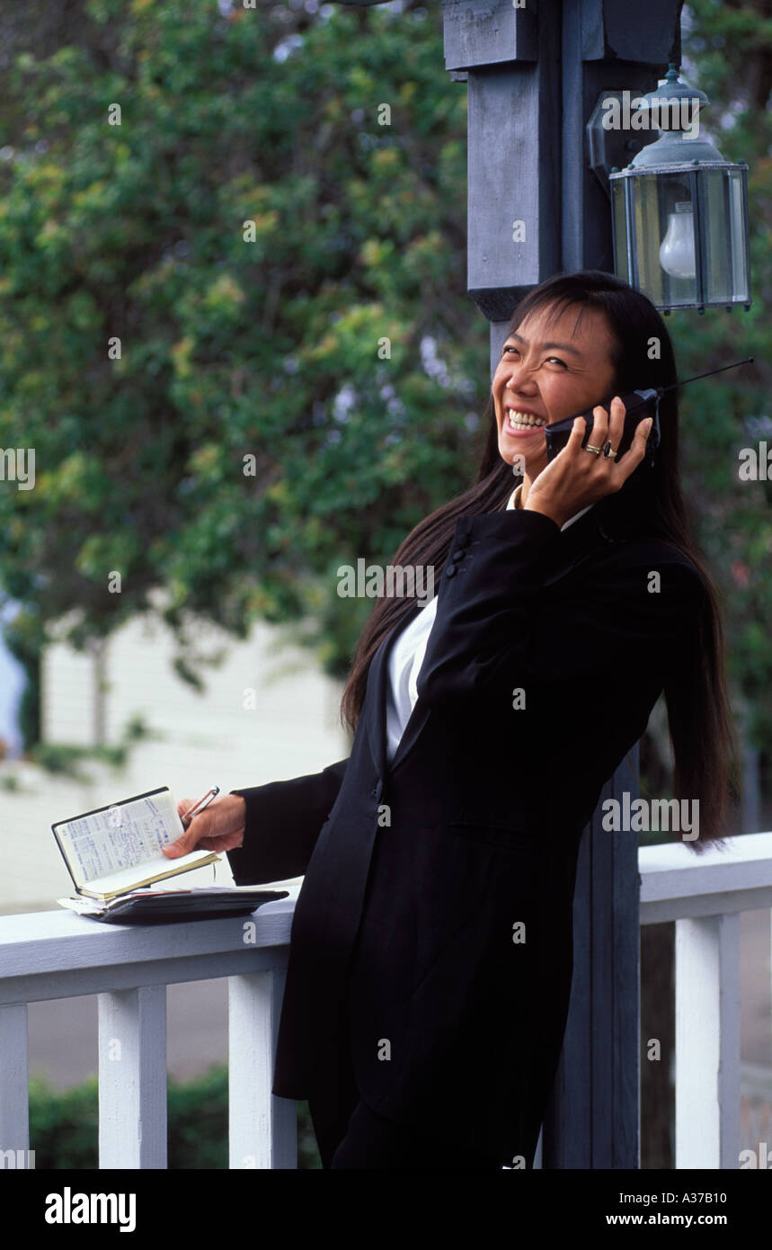 Asian businesswoman using mobile device or cell phone on front porch ...