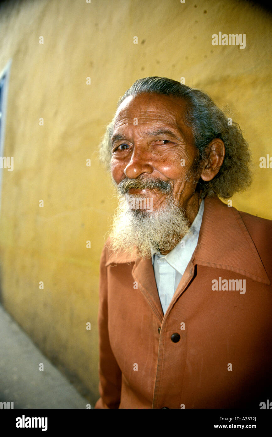 A Cuban man wearing a large collared jacket stands smilig in Old Havana ...