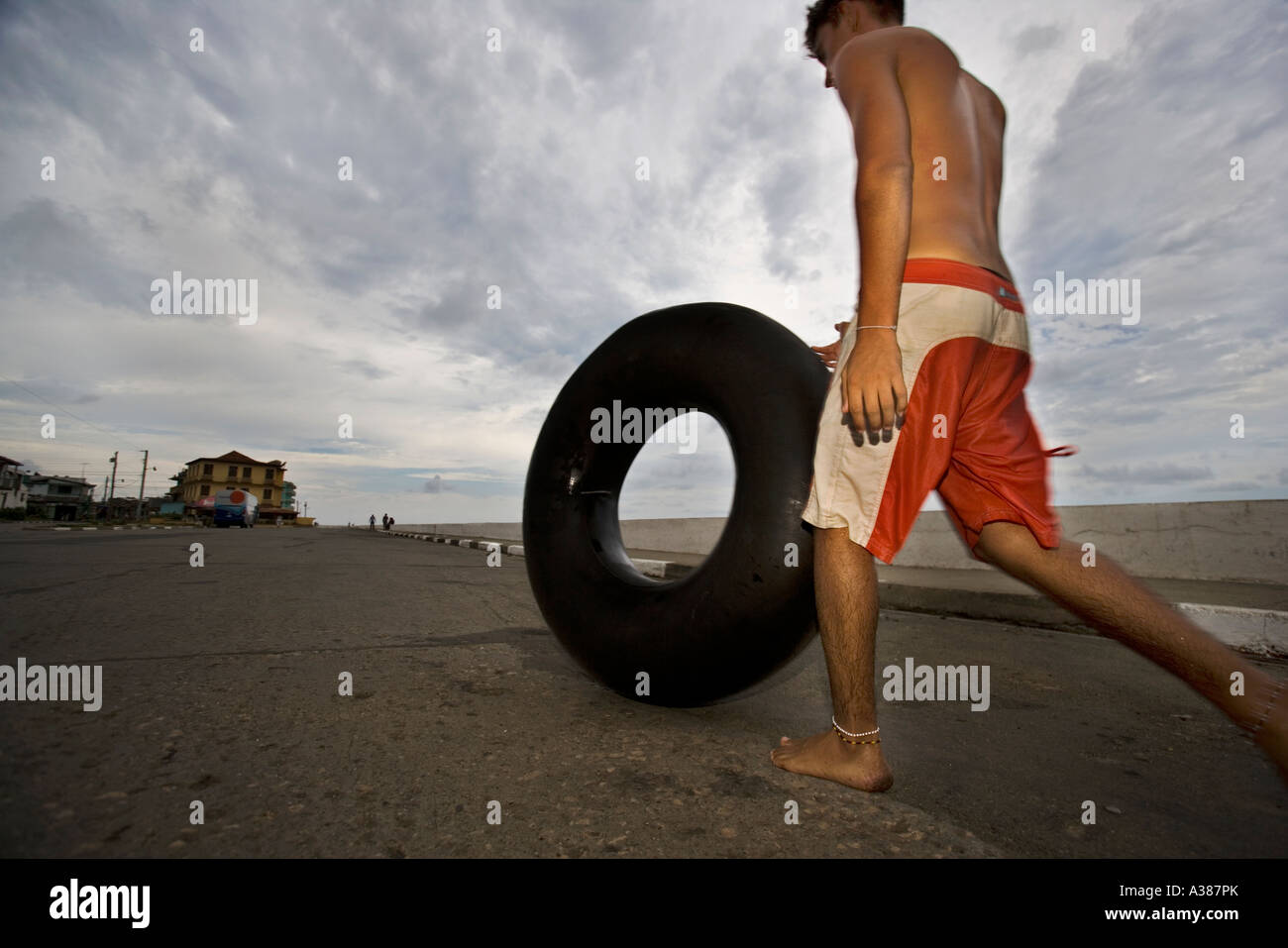 An adolescent Cuban male rolls an inner tube down the sidewalk in ...