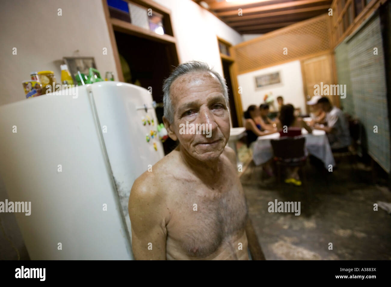 An elderly Cuban man stands in his kitchen while his family eats dinner ...