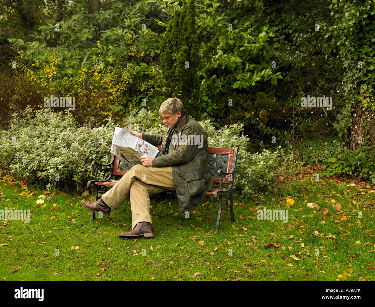 man reading newspaper on park bench Stock Photo - Alamy