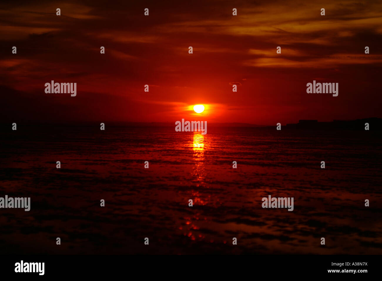 A fiery red sun drops toward the horizon in an intense sunset at dusk ...