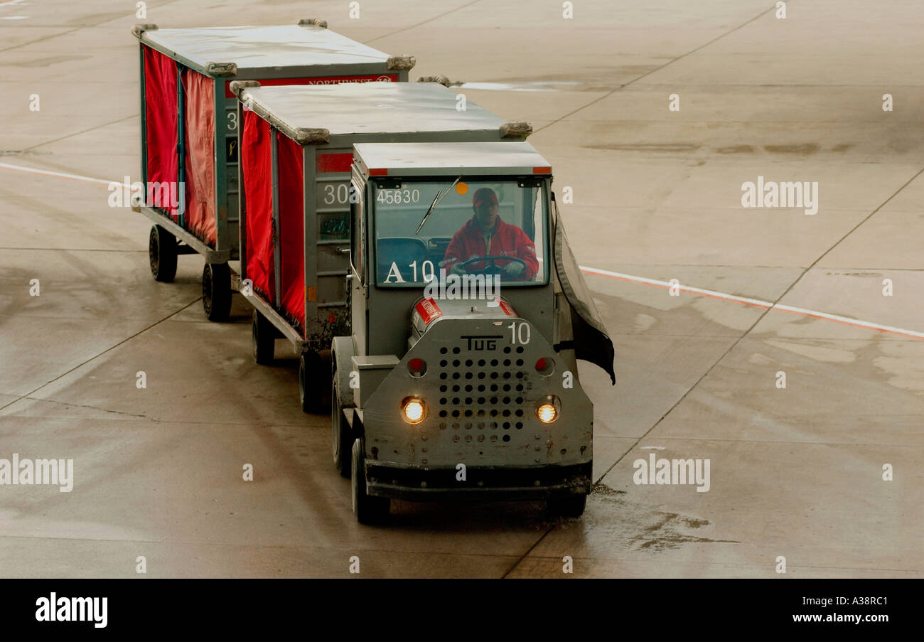 Airport baggage handler driving a baggage truck across airport tarmac ...
