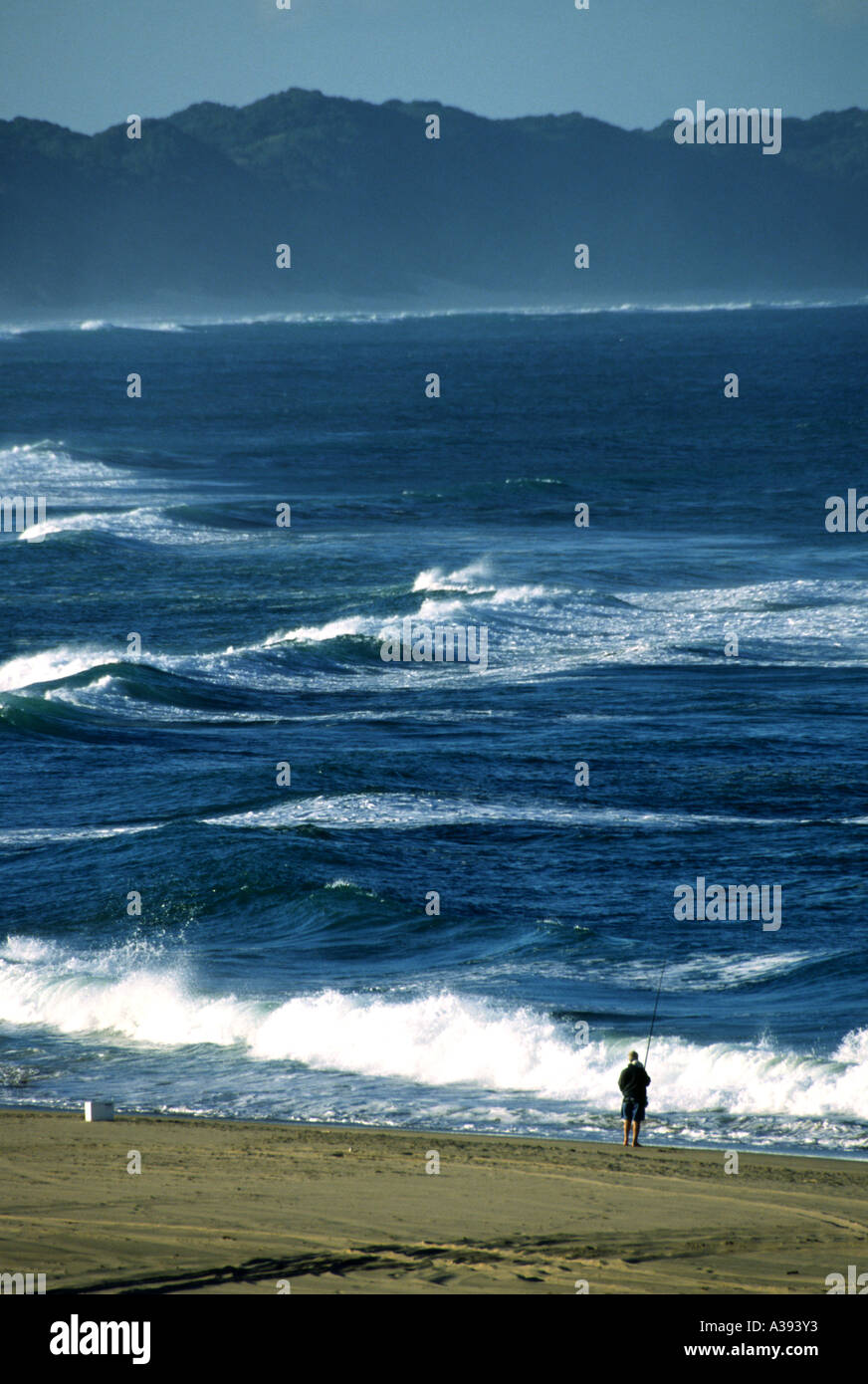Vertical image of surf fisherman on beach with open expanse of blue ...